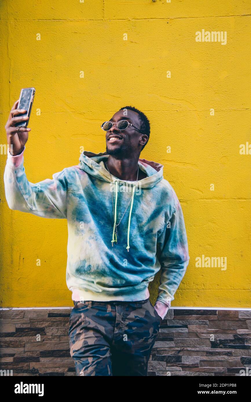 Portrait of smiling young man taking selfie with smartphone in front of ...