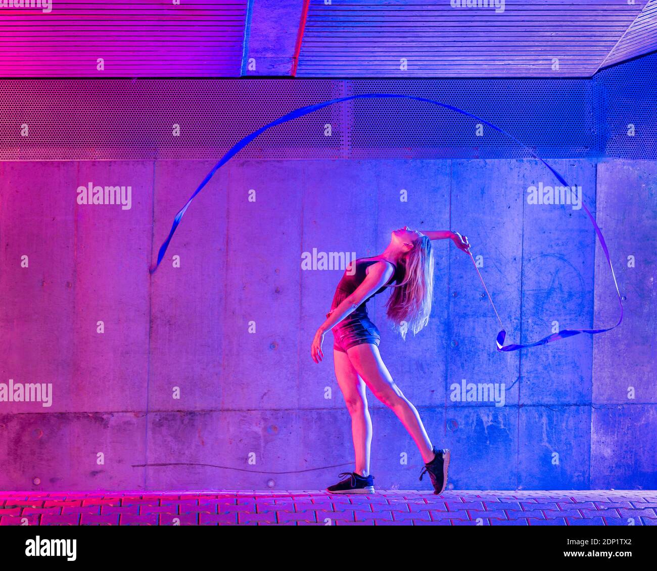 Young woman spinning ribbon while standing against wall Stock Photo - Alamy