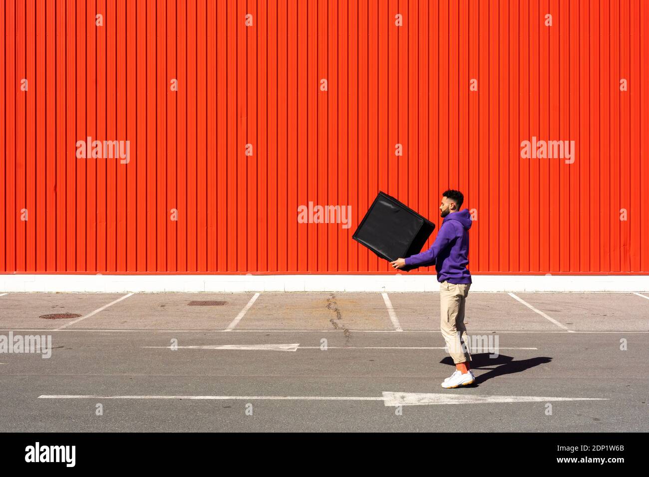 Young man carrying a box in front of a red wall Stock Photo - Alamy