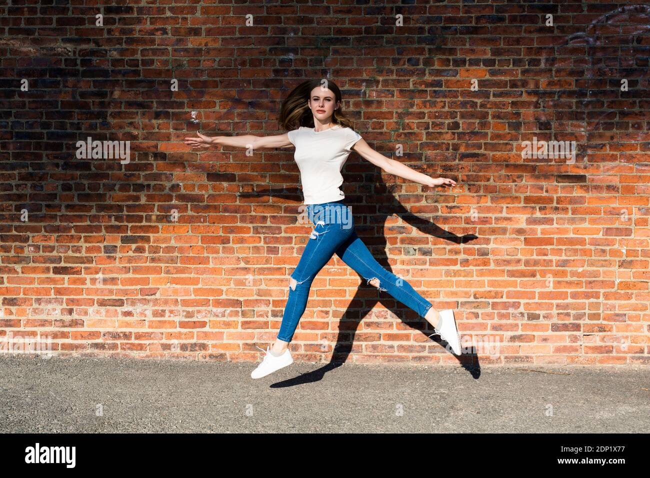 Agile young woman jumping in front of brick wall Stock Photo - Alamy