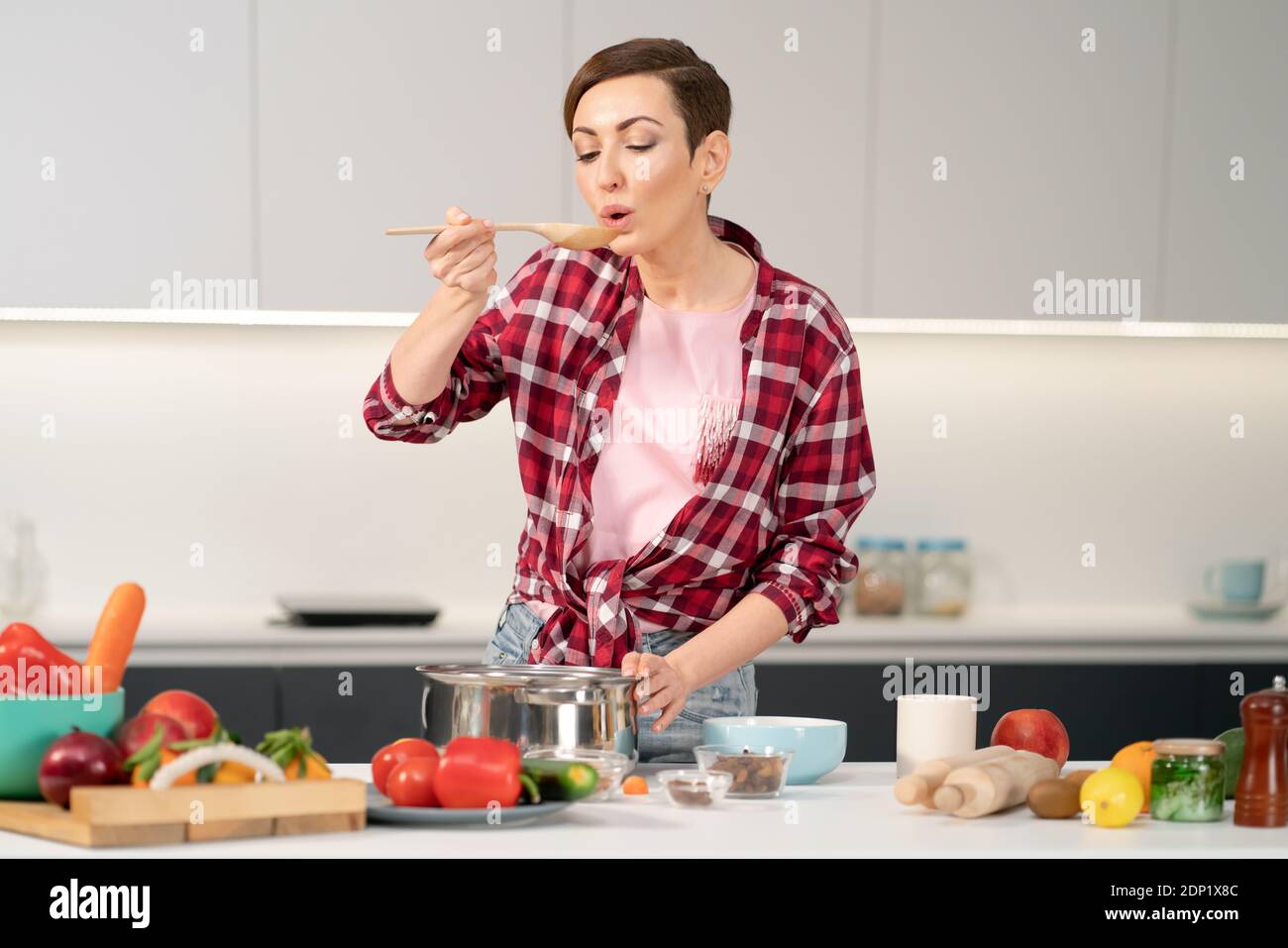 Housewife with a short hairstyle trying a food while she cooking lunch ...