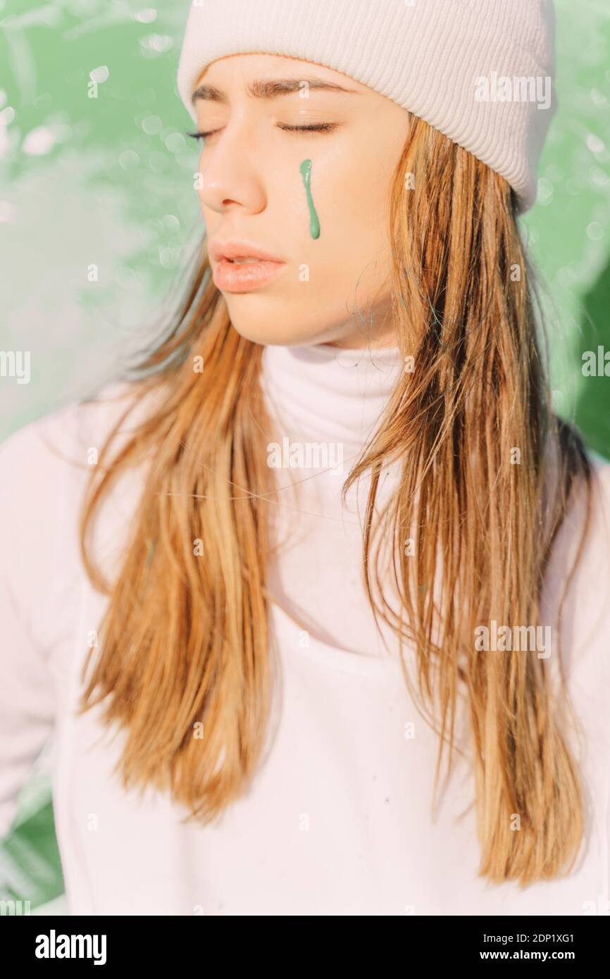 Young woman standing in front of green canvas with green tear on her ...