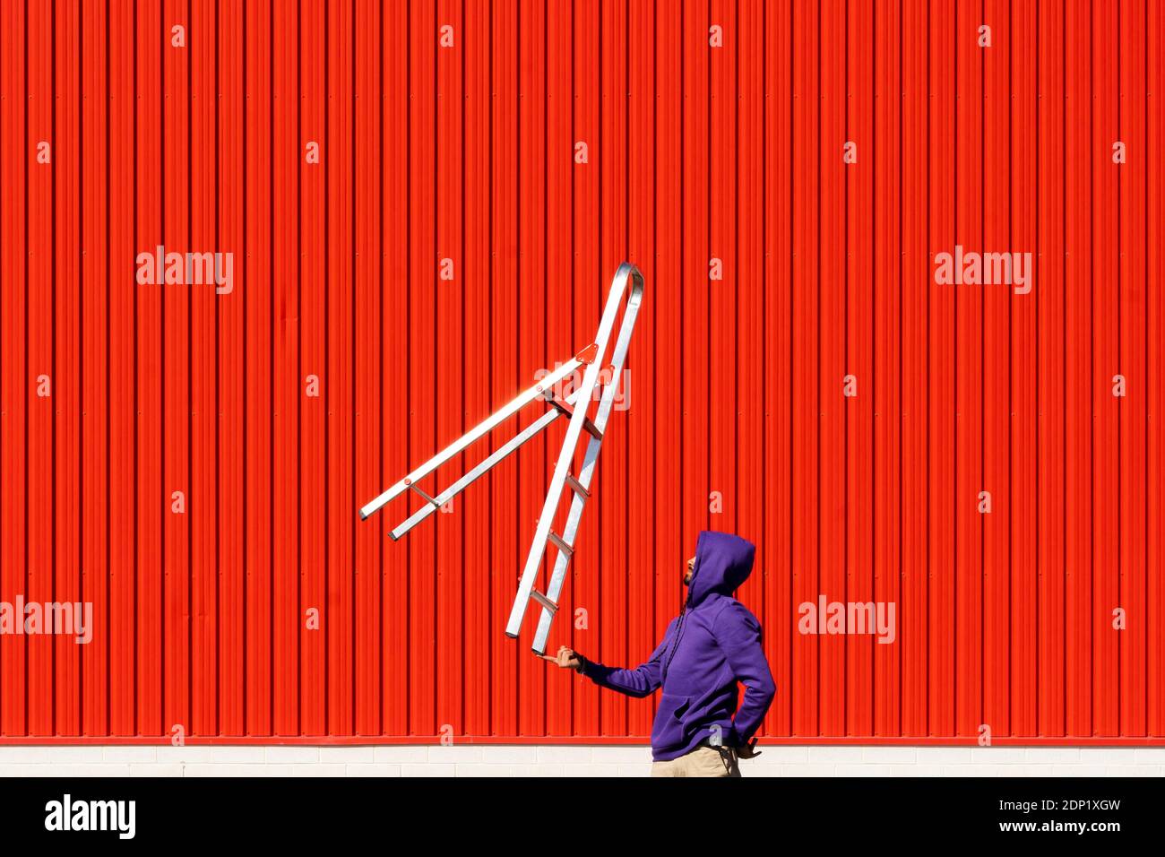 Young man balancing a ladder in front of a red wall Stock Photo - Alamy