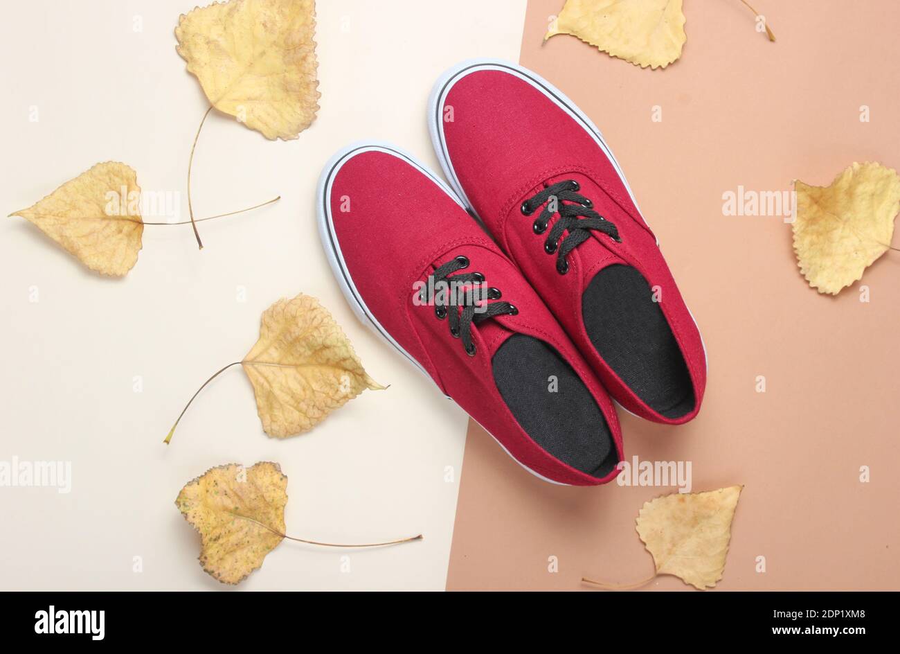 Red sneakers and fallen autumn leaves on a beige paper background ...