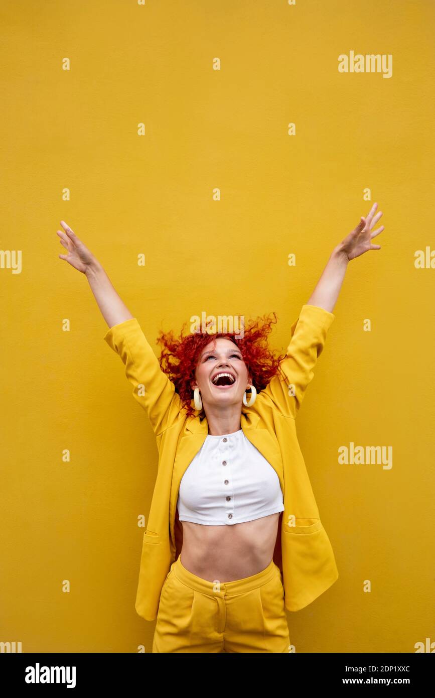 Exuberant young woman with red curly hair laughing in front of yellow ...