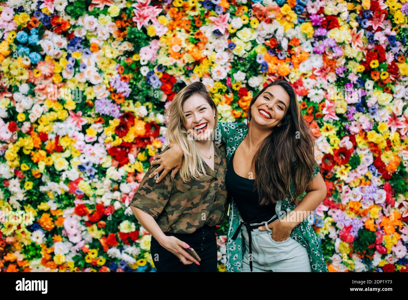 Cheerful beautiful female friends standing against colorful flowers ...