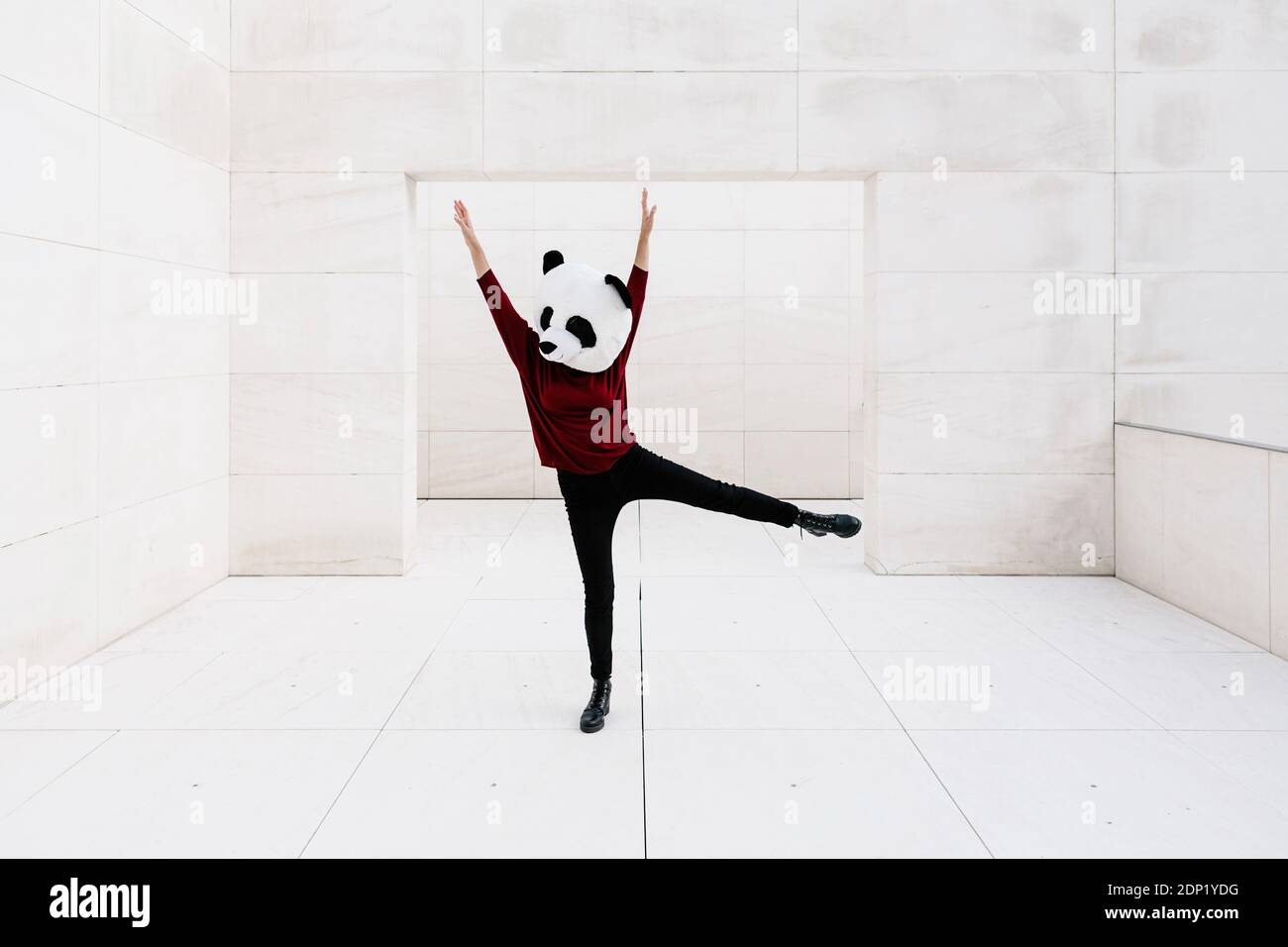 Woman wearing panda mask with arms raised standing against doorway ...