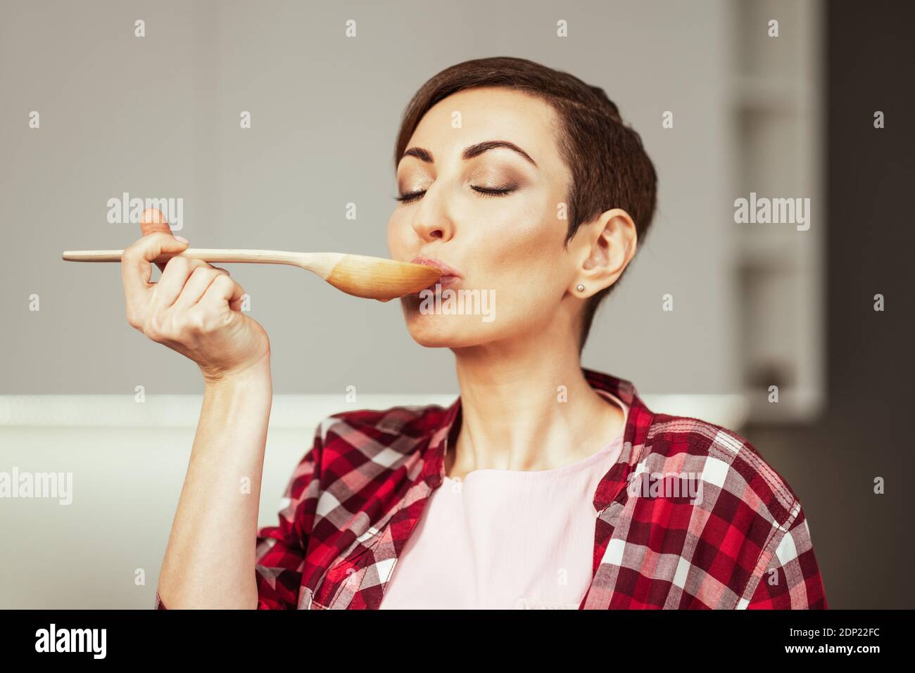 Mother with a short hairstyle testing a food while cooking a dinner for ...