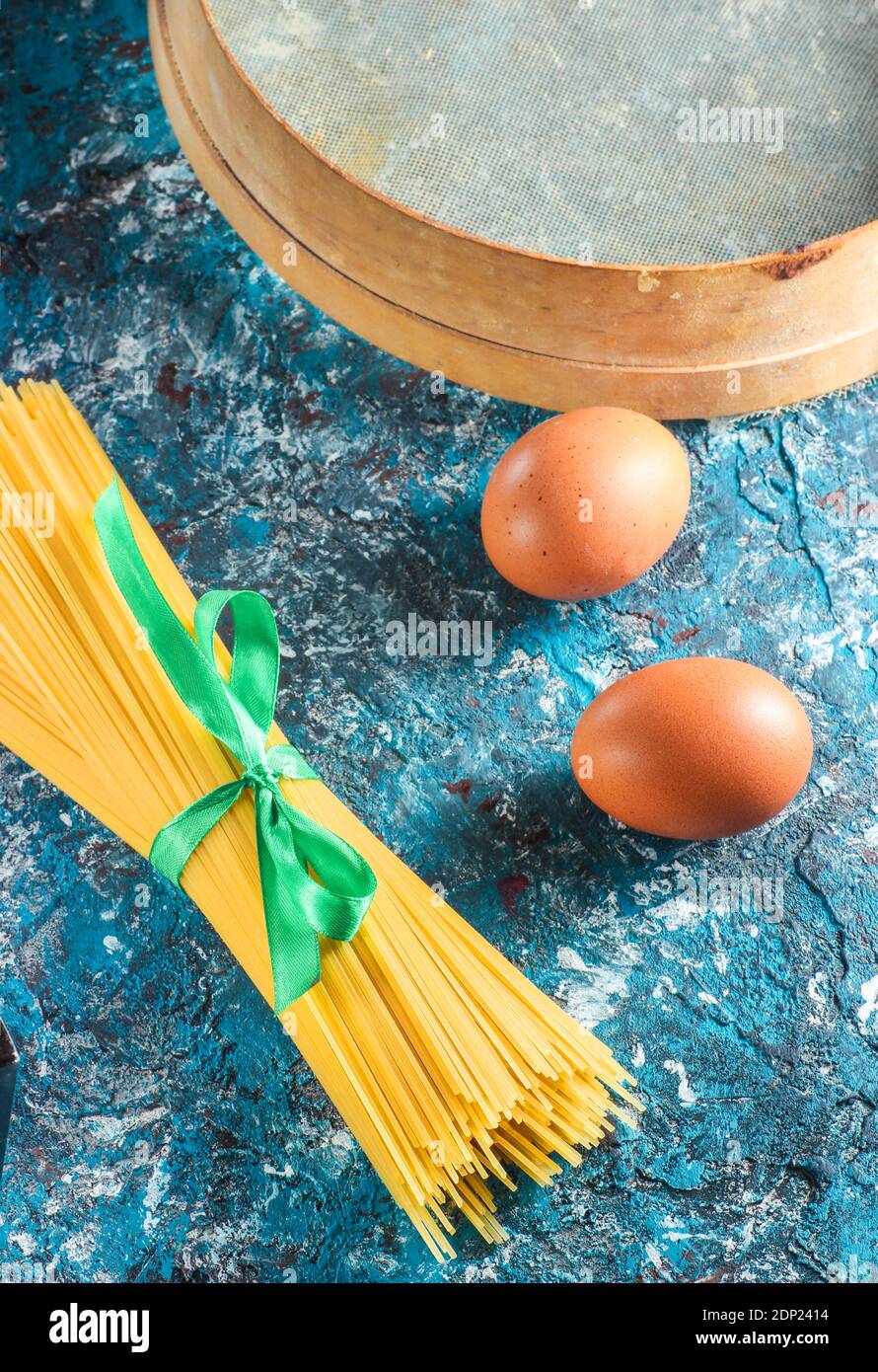 Italian pasta, sieve, eggs on a blue concrete background. Cooking ...