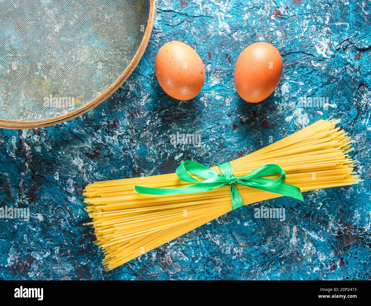 Italian pasta, sieve, eggs on a blue concrete background. Cooking ...