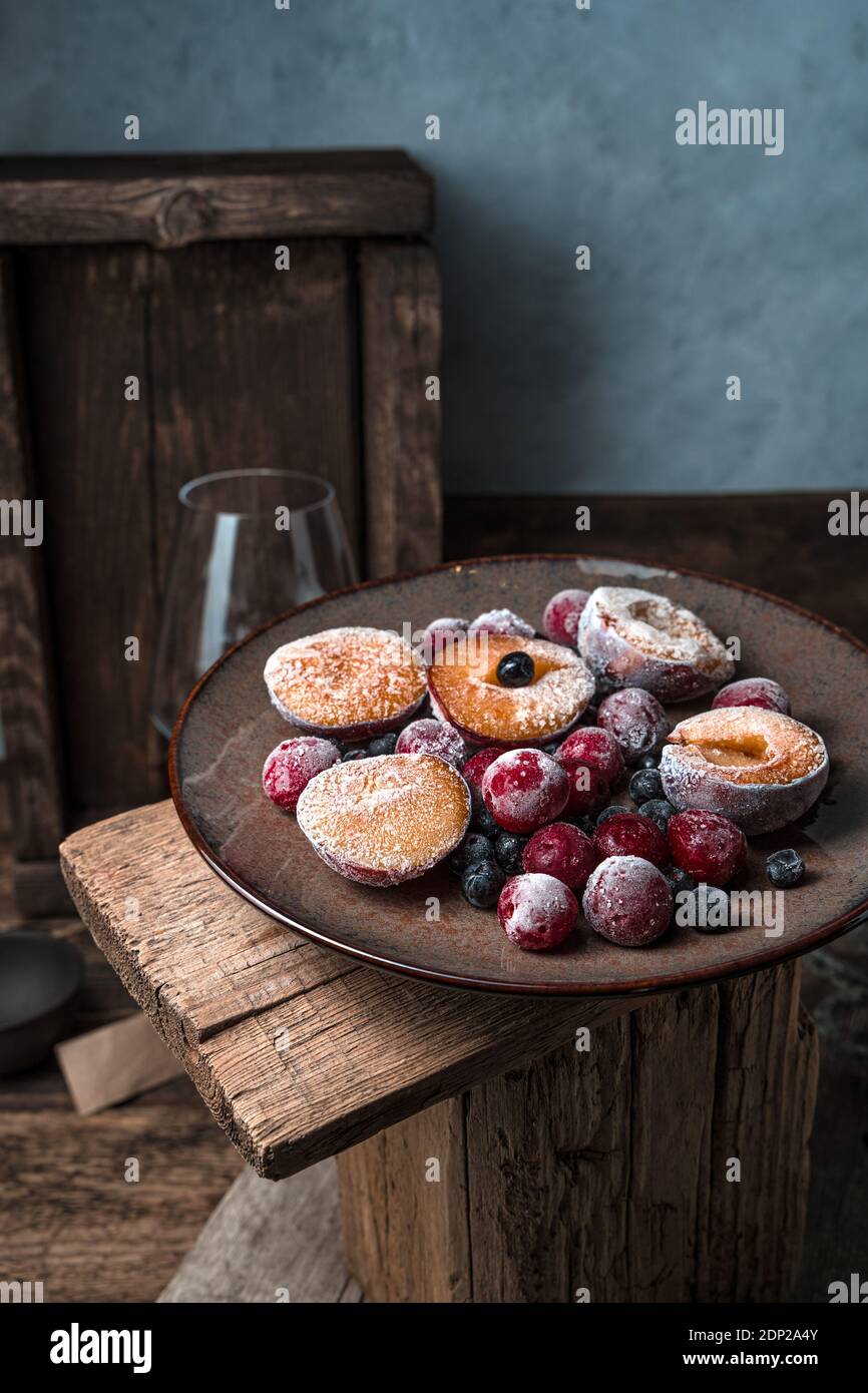 Still life with frozen berries and fruits in a brown plate on a vintage ...