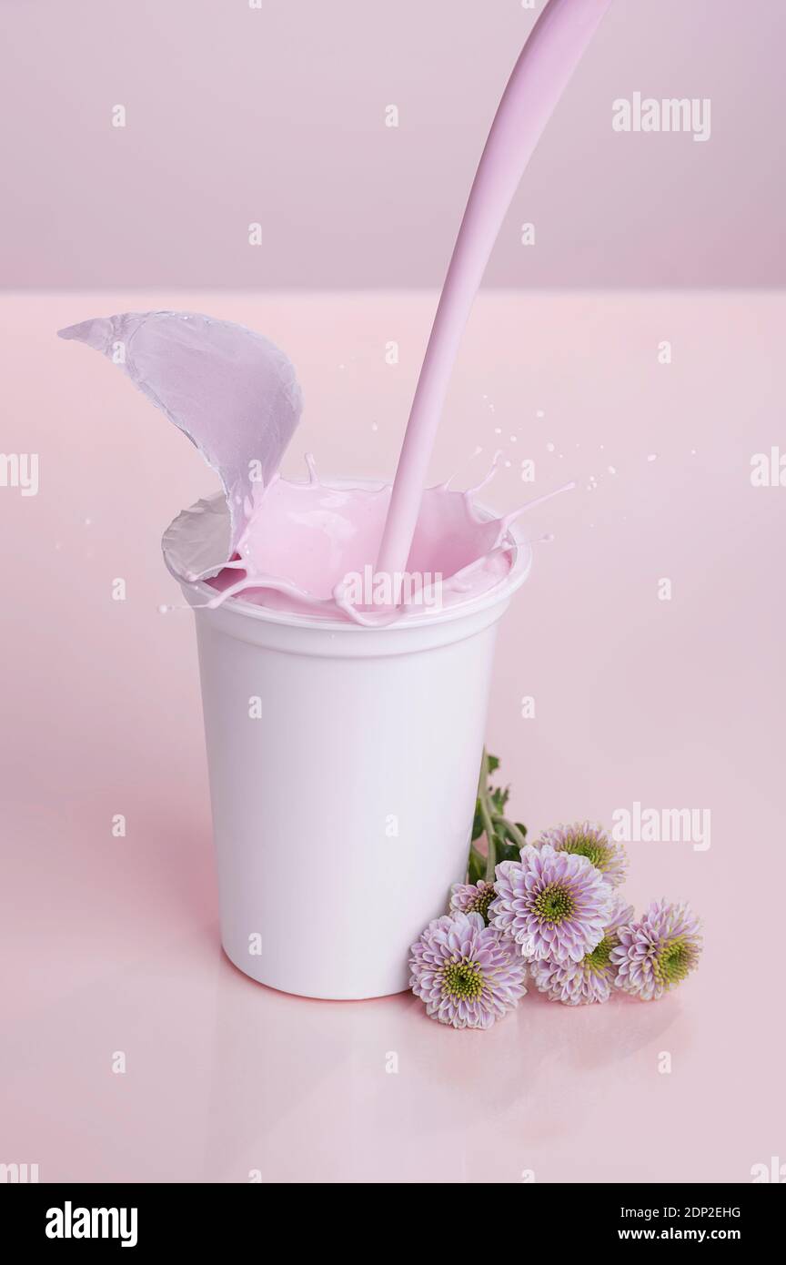 A Generic, white, plastic cup of pink yoghurt on a pink background with ...