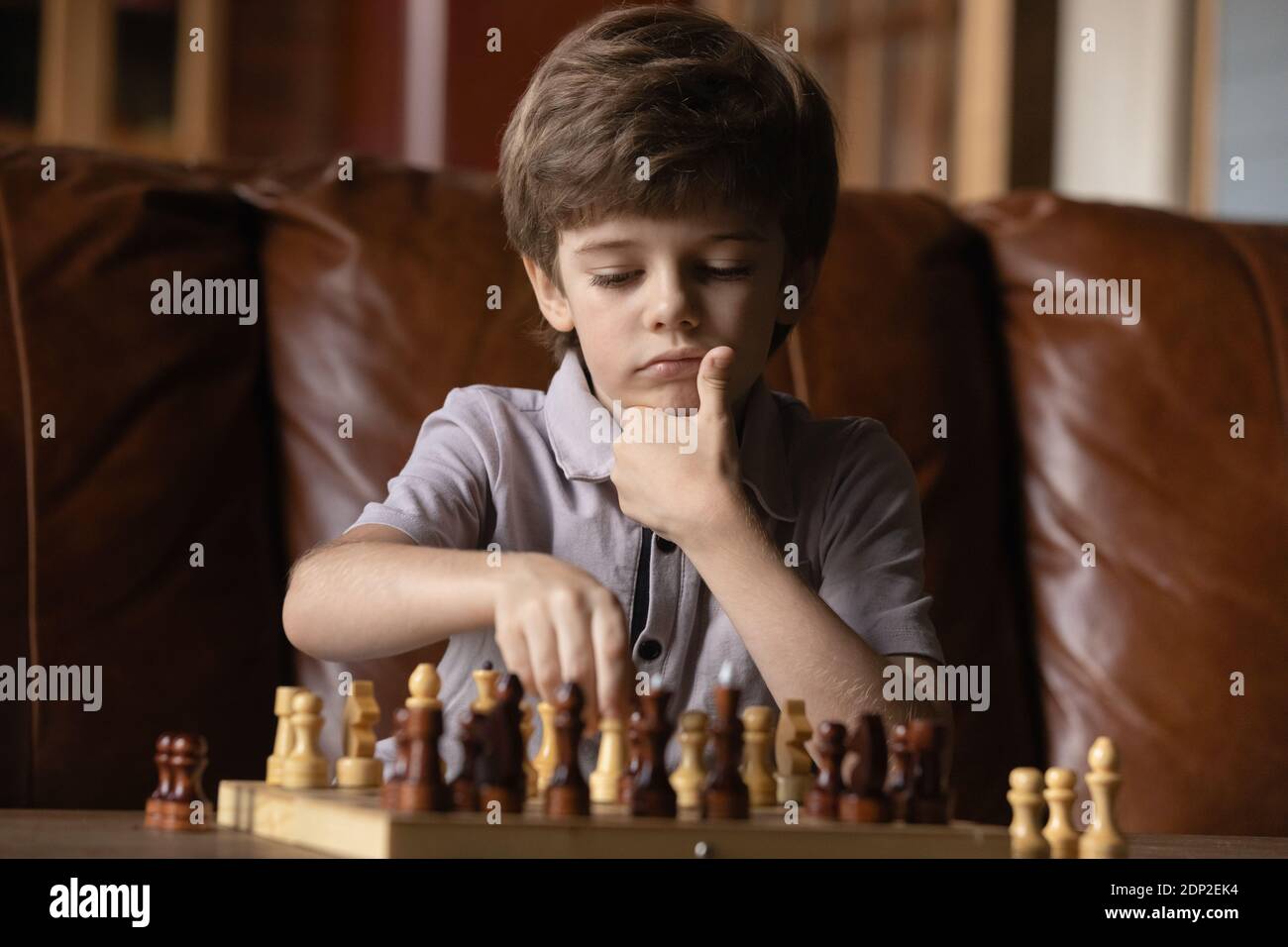 Thoughtful little boy sitting on couch by chessboard playing chess ...