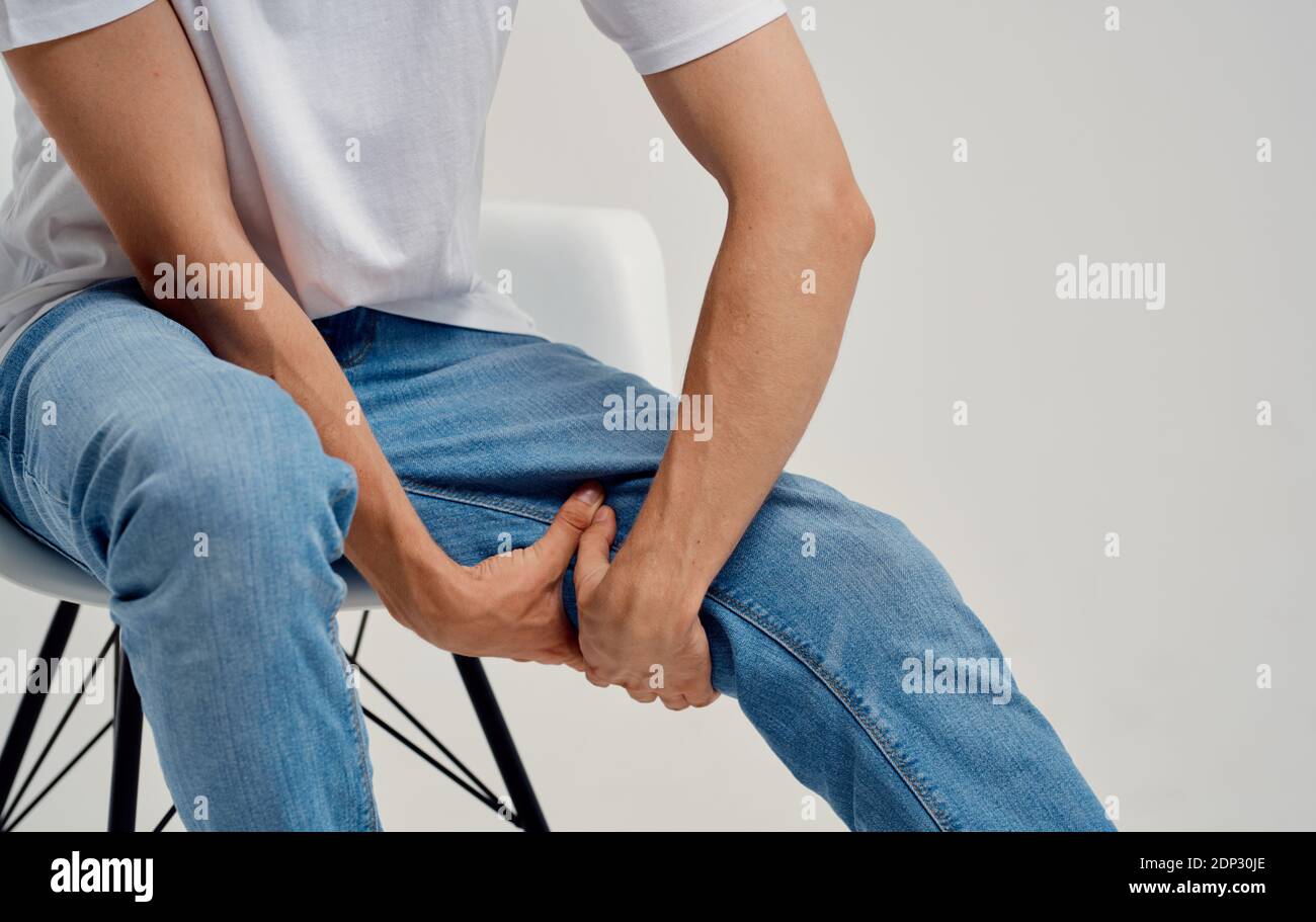 man in jeans sitting on a chair and touching his leg with his hands ...
