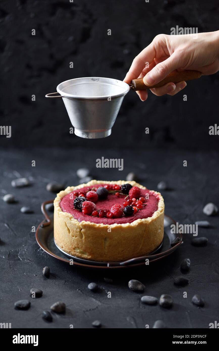 Healthy homemade pastry. Woman hand pouring icing sugar on lingonberry ...