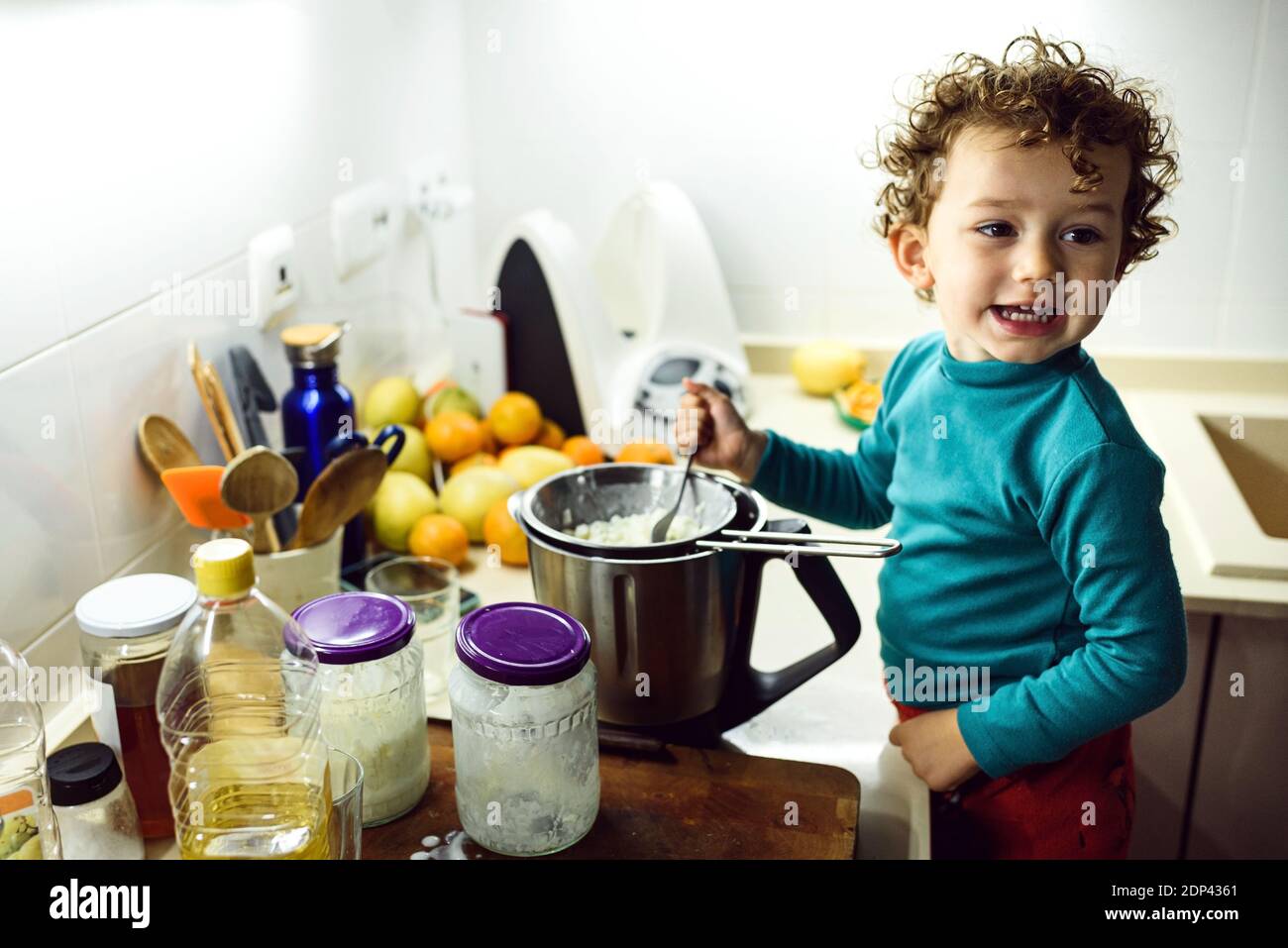 Little curly-haired girl plays cooking in a real kitchen with natural ...