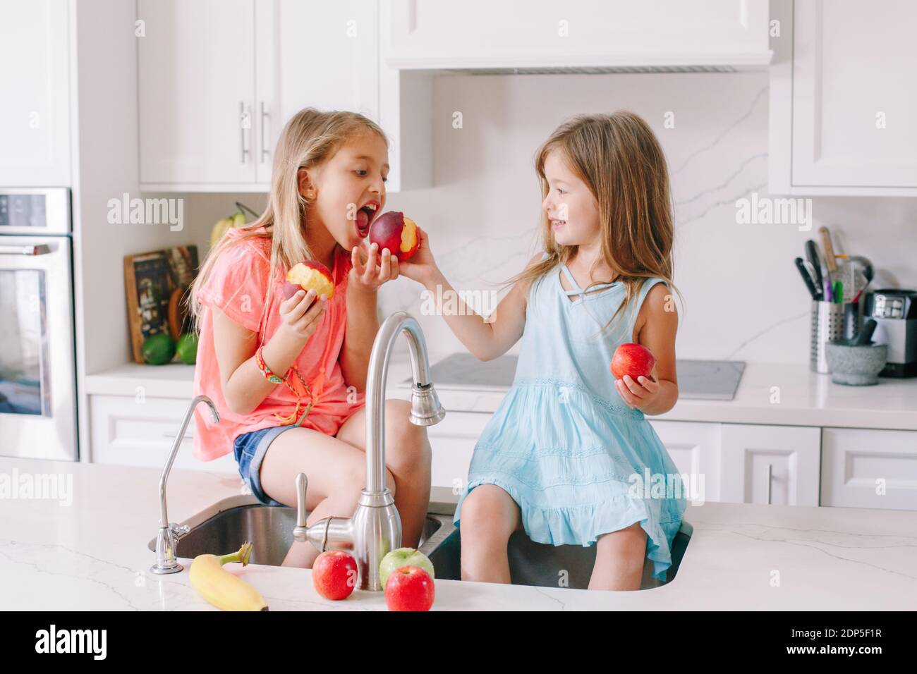 Caucasian children girls eating sharing fresh fruits sitting in kitchen ...