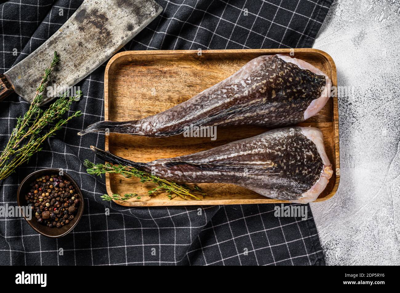 Fresh monkfish without a head on a wooden tray with a cleaver. Gray ...