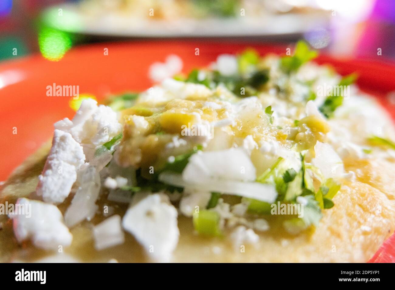 Tlacoyo with cheese, green sauce, and sour cream on a red plate Stock ...