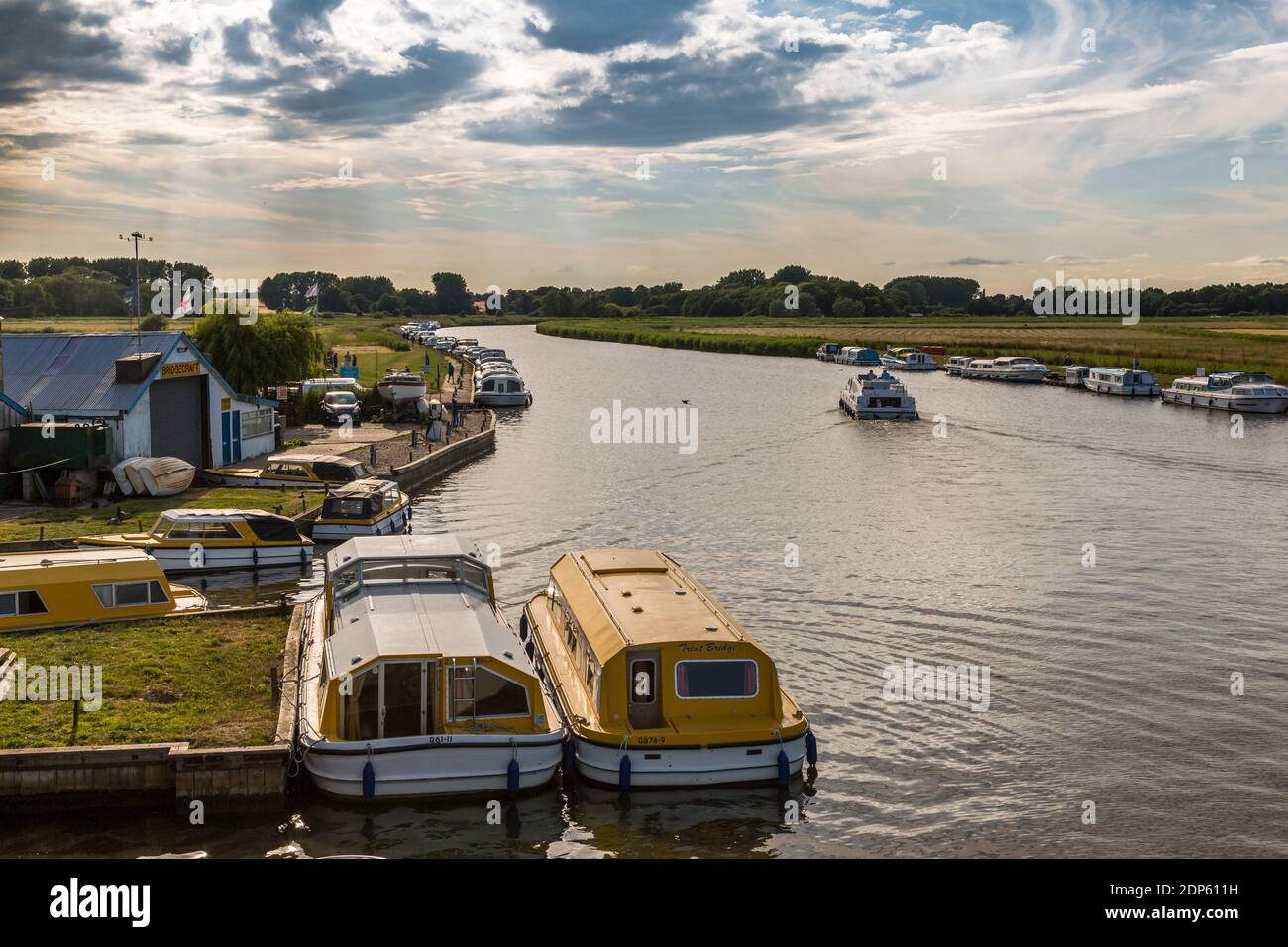 Rays of sunshine through broken clouds and boats on River Bure at Acle ...