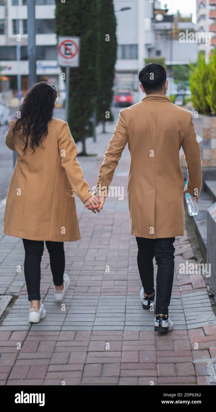 A vertical shot of a couple wearing beige coats holding hands and ...