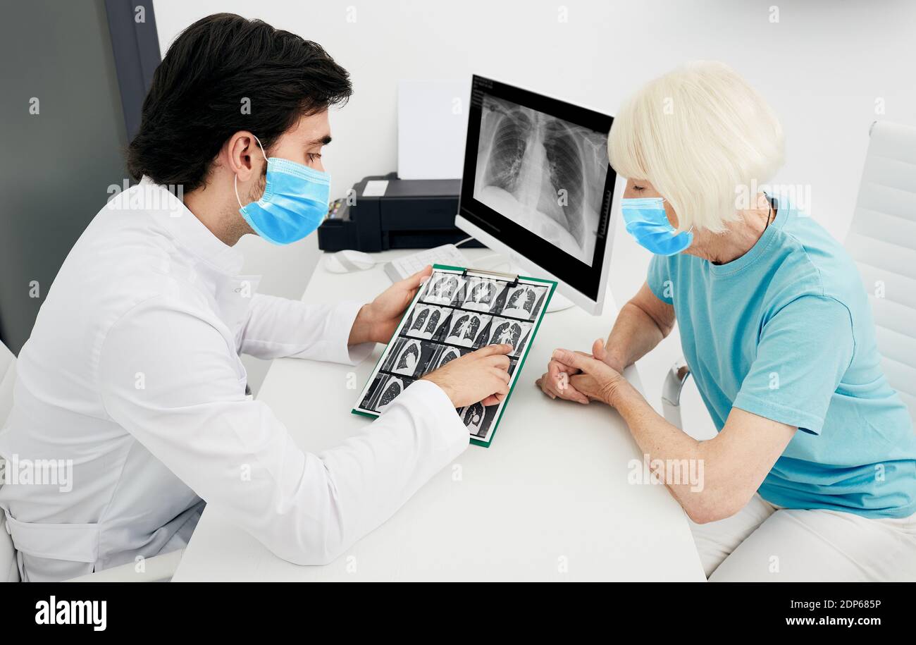 Pulmonologist wearing a protective mask showing a senior patient a CT ...