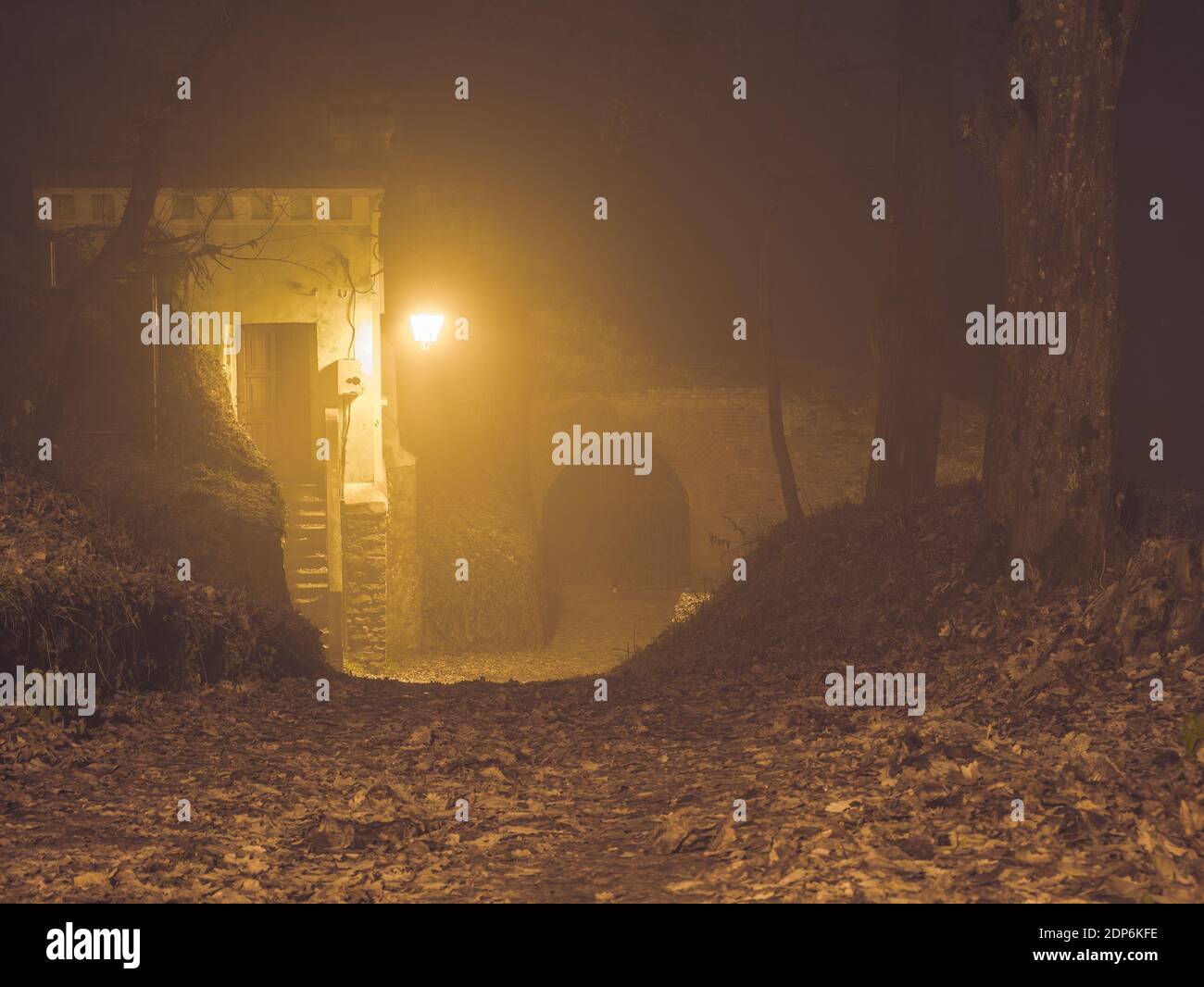 Lamp post in a foggy night hanging from a medieval stone wall. Dark and ...
