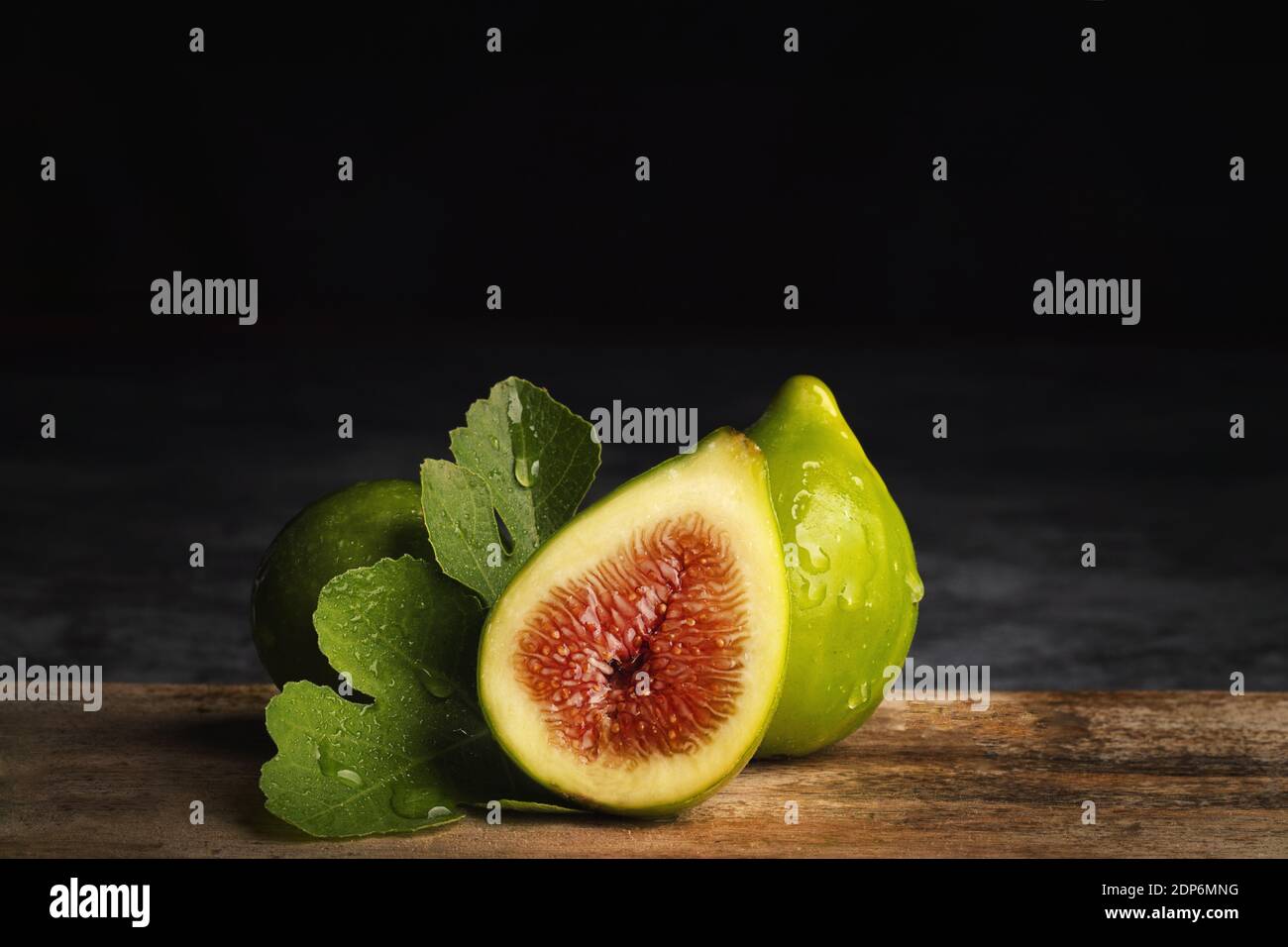 Fresh whole fig fruit and a half fig on a wooden board on a black ...