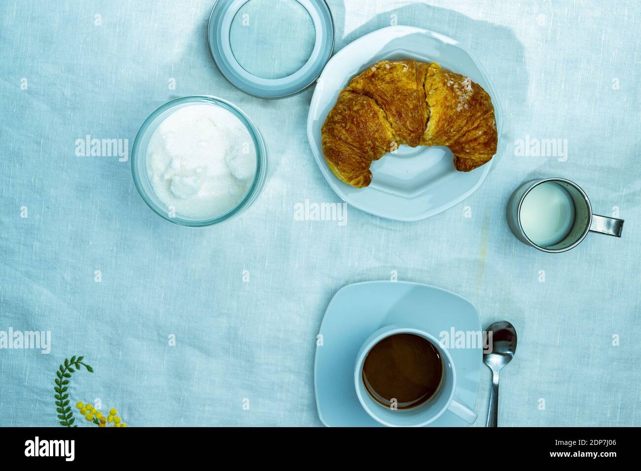 A top view closeup of a croissant on a white plate next to a container ...