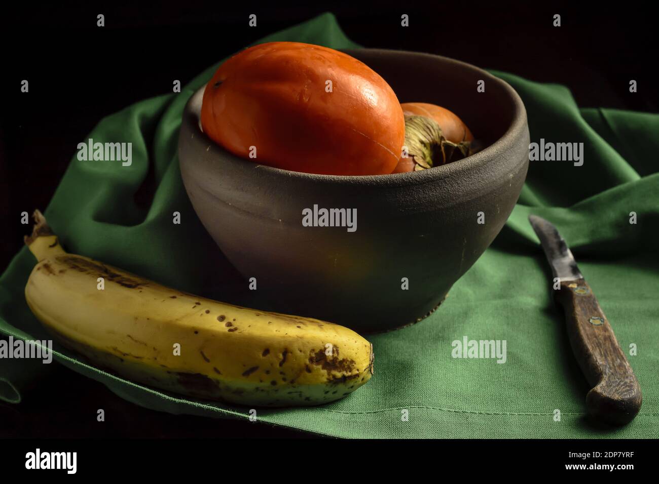 A vertical closeup of persimmons in a handmade clay container, a banana ...