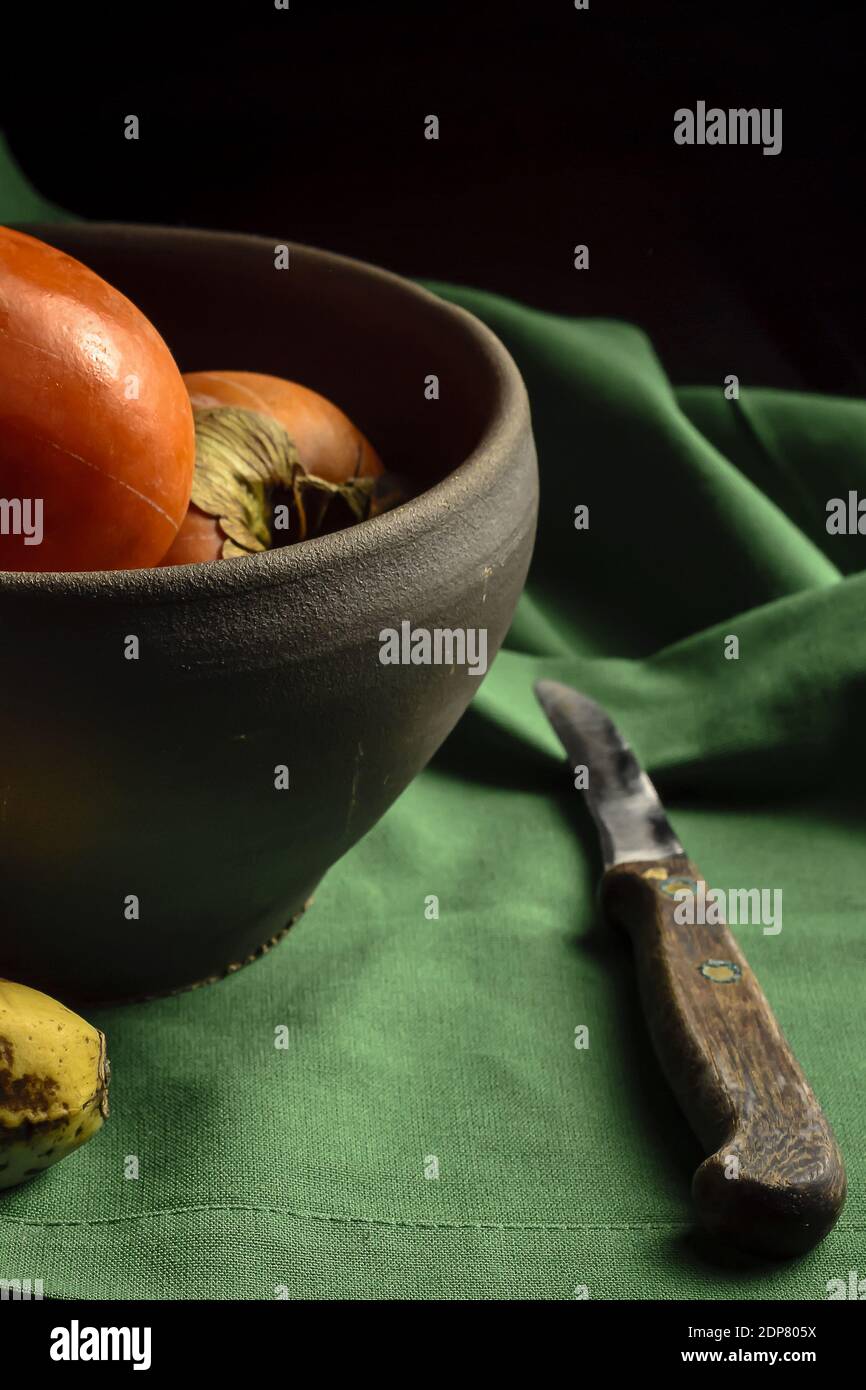 A vertical closeup of persimmons in a handmade clay container, a banana ...