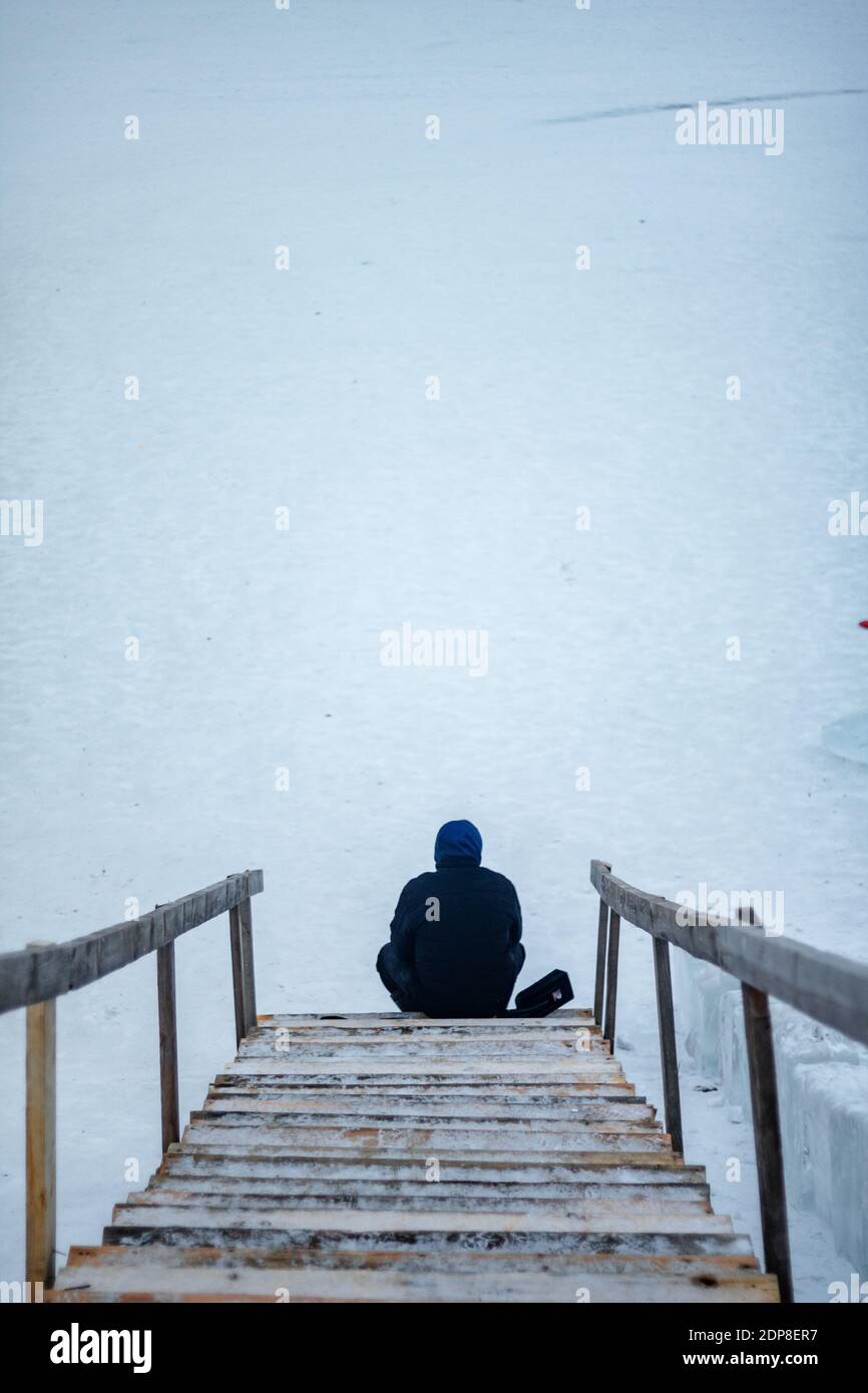 Man sitting alone on wooden bridge, vertical Stock Photo - Alamy