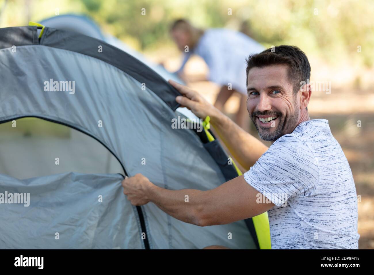 two cheerful young men setting up a tent Stock Photo - Alamy