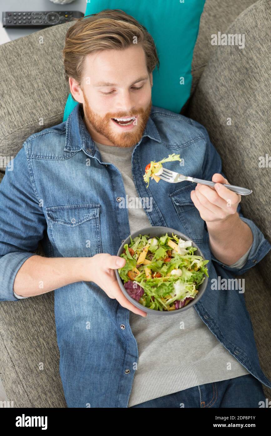 man eating a healthy salad lying on his couch Stock Photo - Alamy