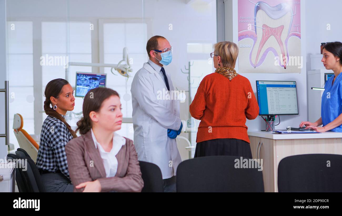 Dentistry doctor talking with senior woman standing in reception area ...