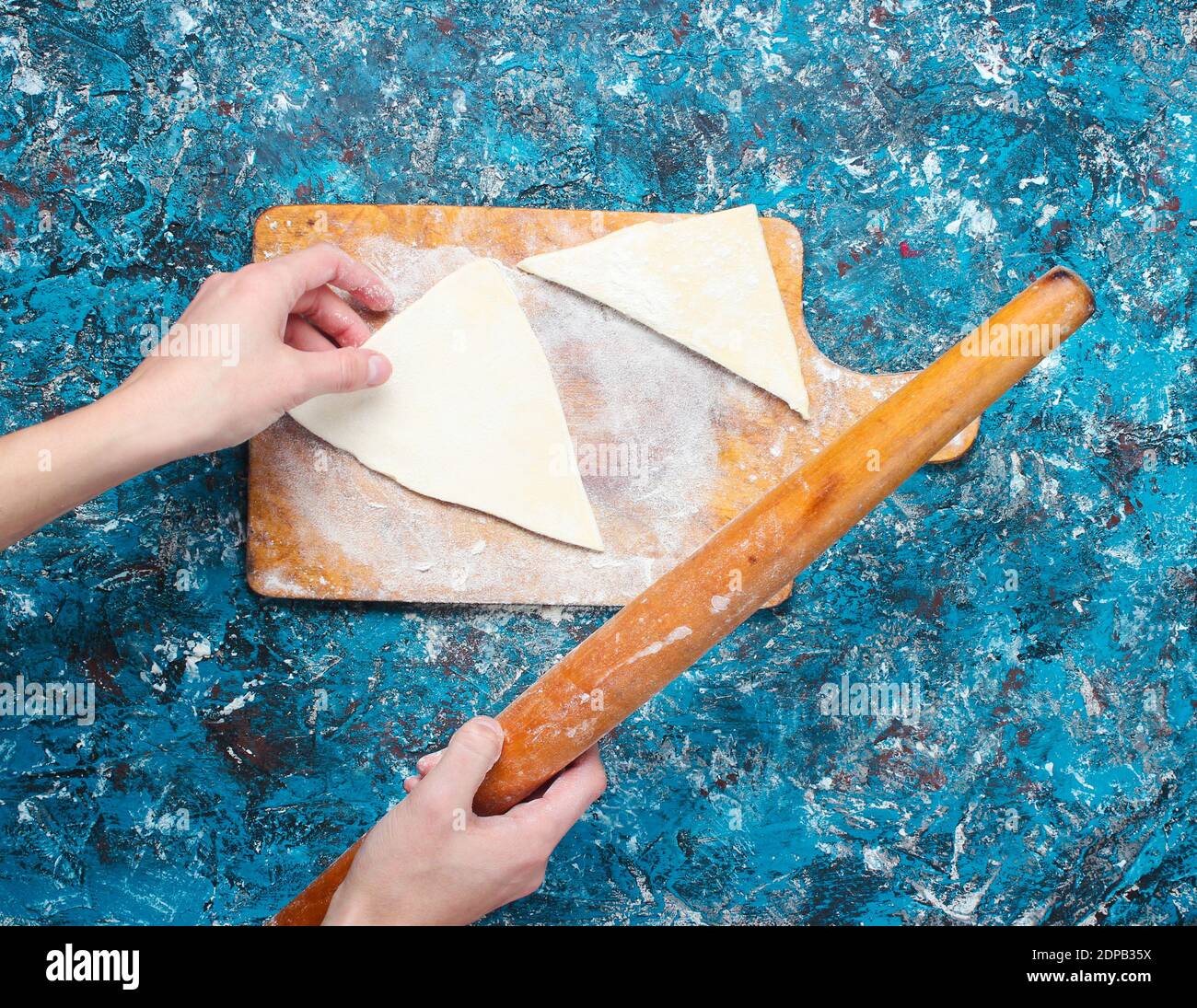 Hands keep rolling pin and roll the dough on blue concrete table ...