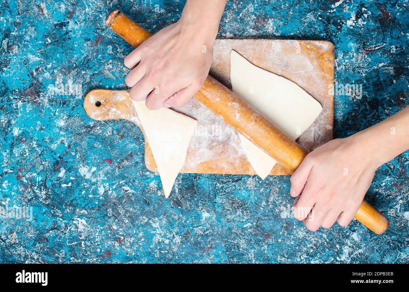 Hands keep rolling pin and roll the dough on blue concrete table ...