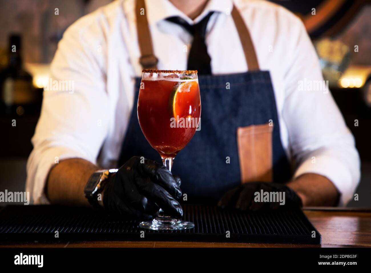 Detail of the hands of a bartender with black gloves placing a crystal ...