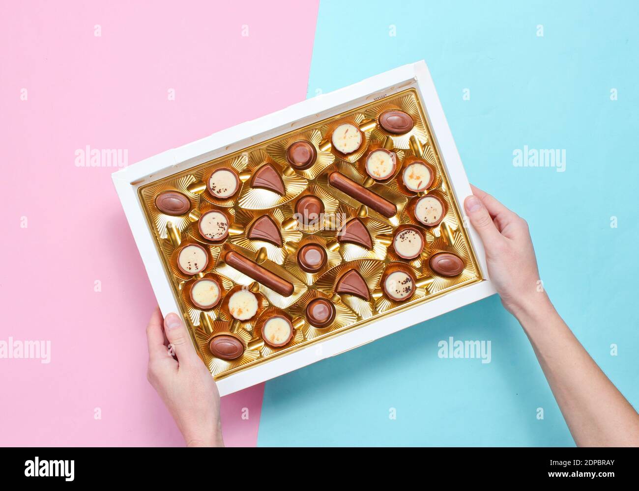 Girl holding her hands a box of chocolates in a golden tray on a pastel ...