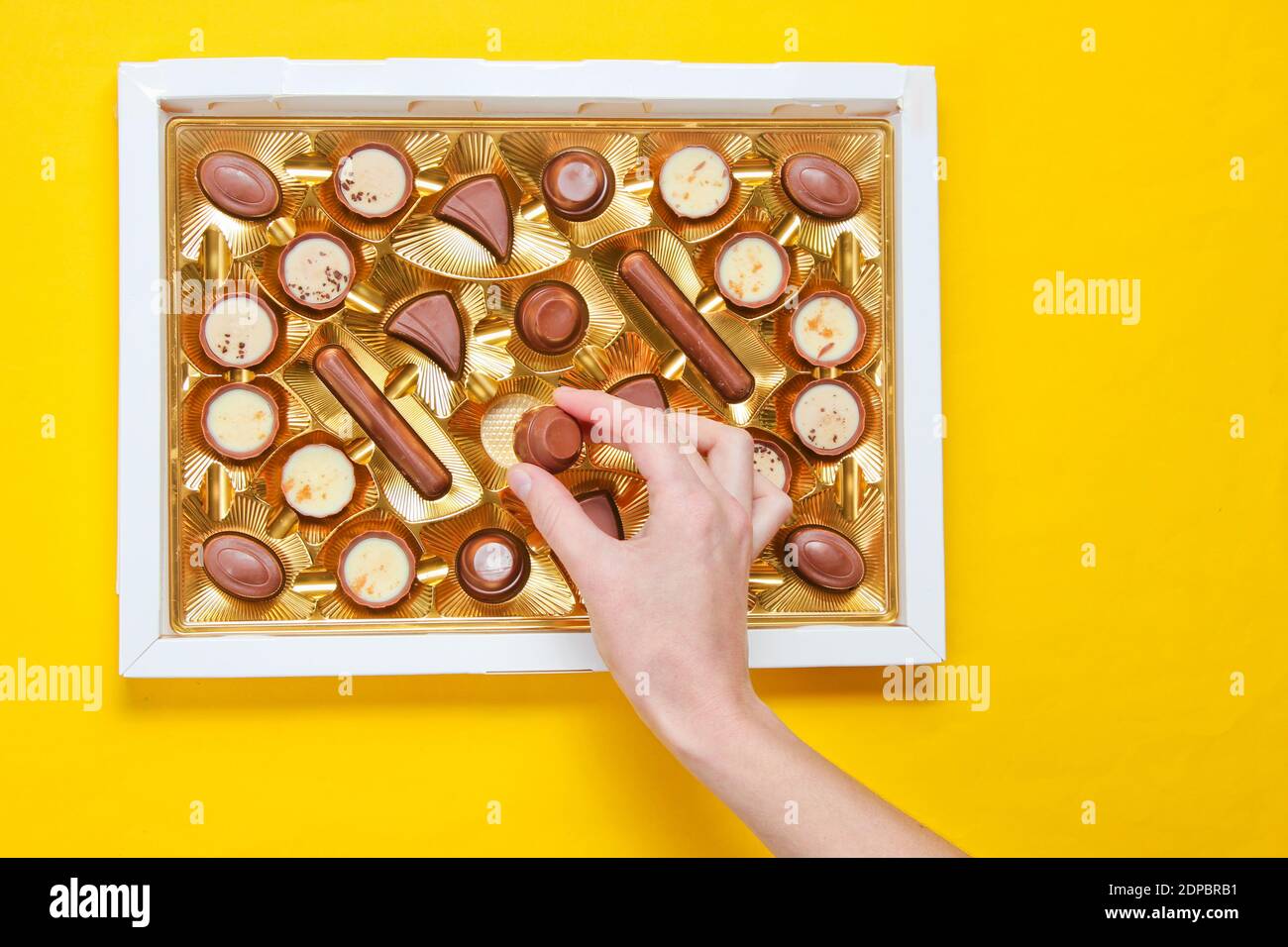 Girl takes a chocolate candy from a box of chocolates with a golden ...