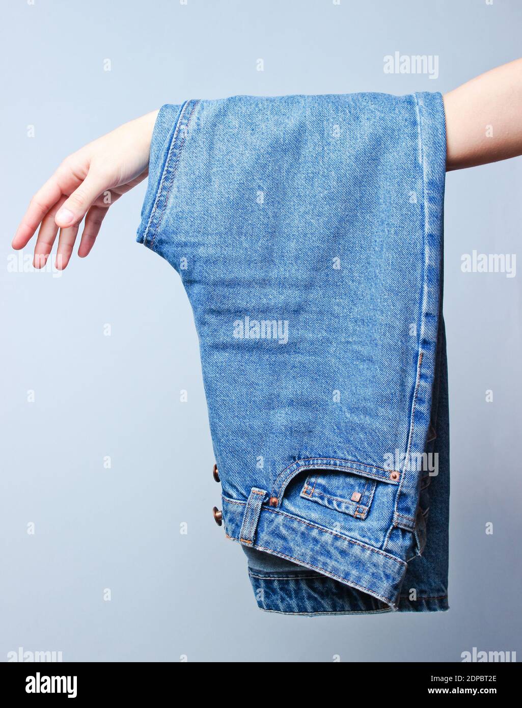Blue jeans hanging on a female hand on a gray background. Front view ...