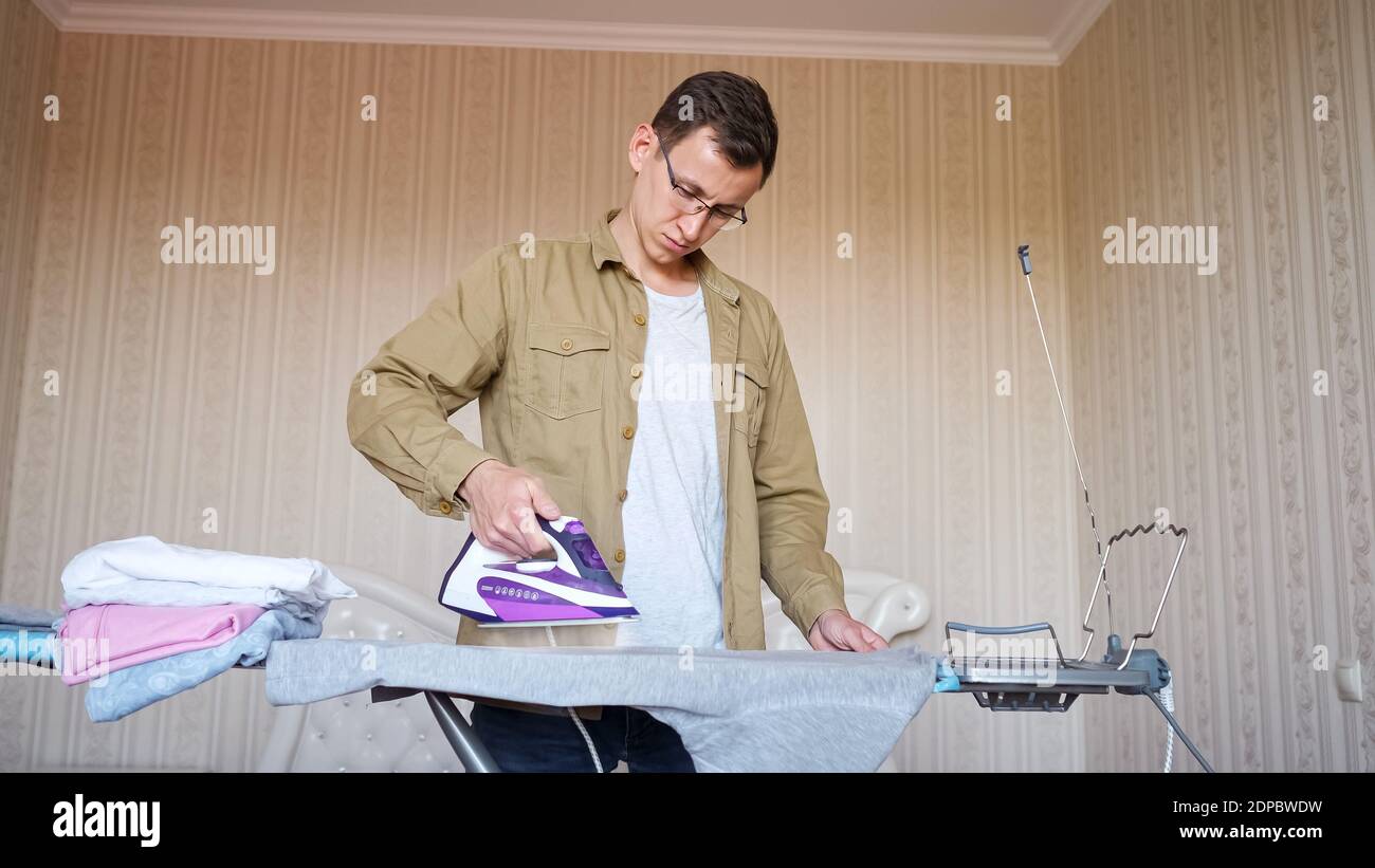 Young man in glasses and shirt ironing things on an ironing board Stock ...