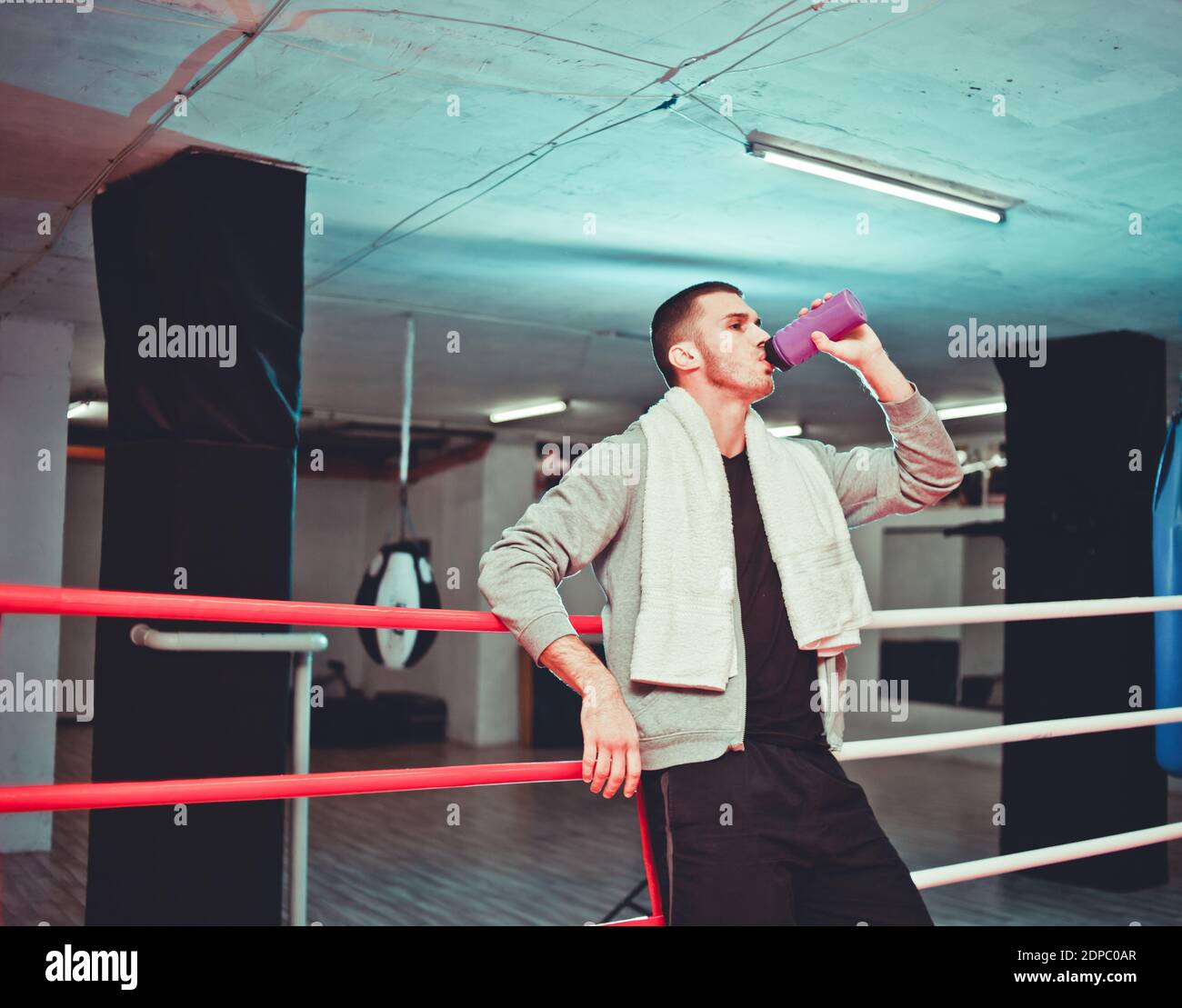 Rest boxer in the ring. Young man in hooded sweater drinks water from ...