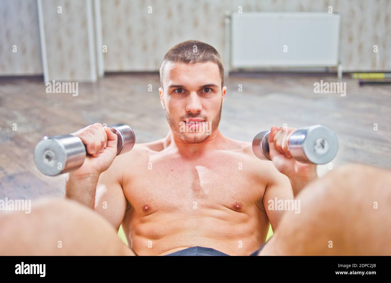 Young handsome man doing a curl for abdominals with dumbbells in his ...