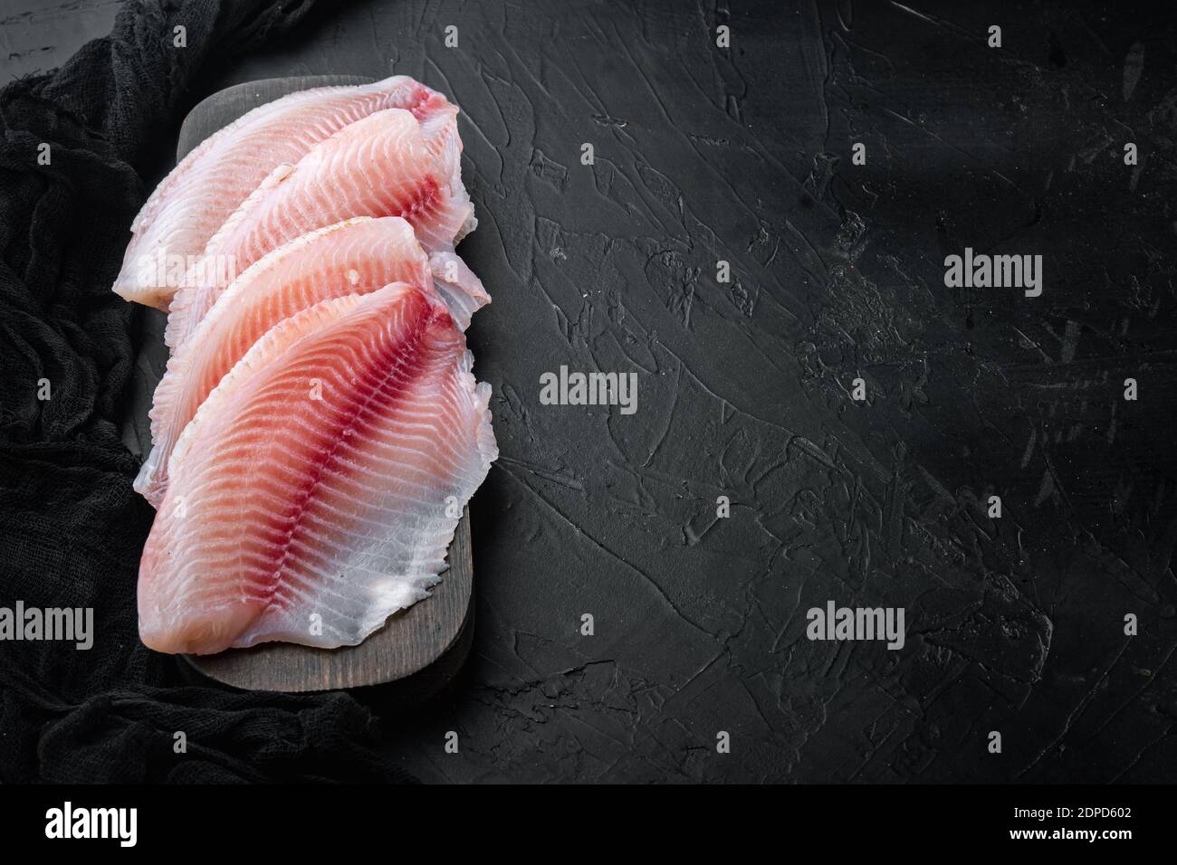 Tilapia fish, skinless meat, on black background with copy space for ...