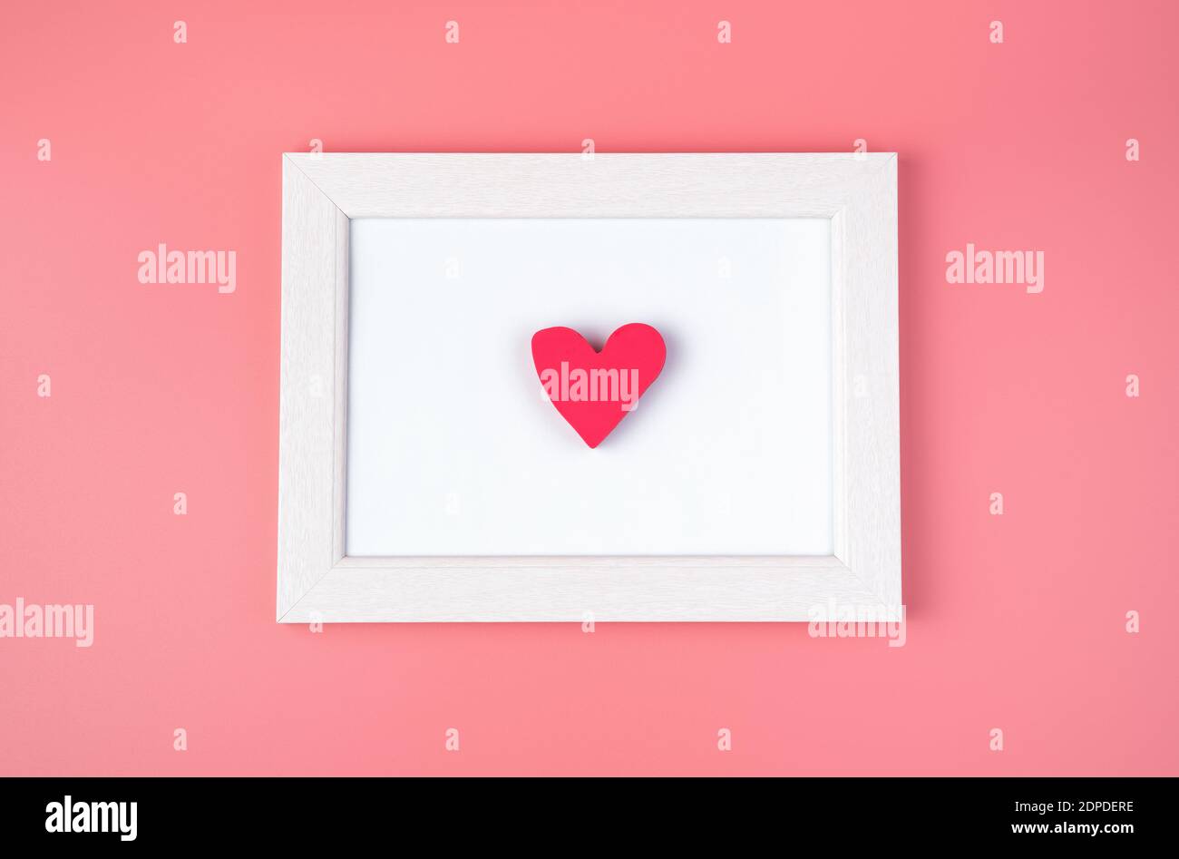 White rectangular frame with a red heart in the center on a pink ...