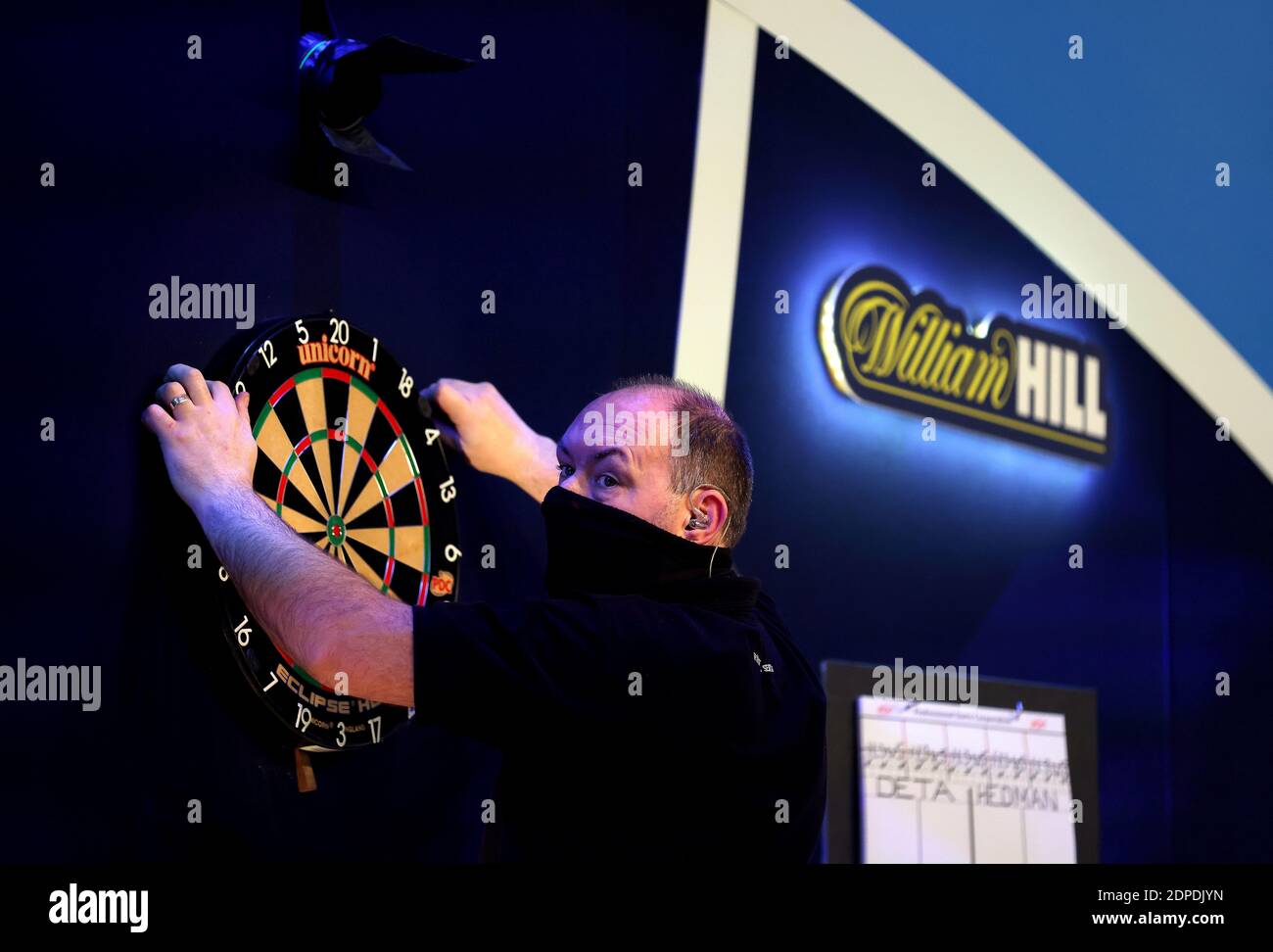 An official wearing a face mask replacement the dartboard ready for the ...