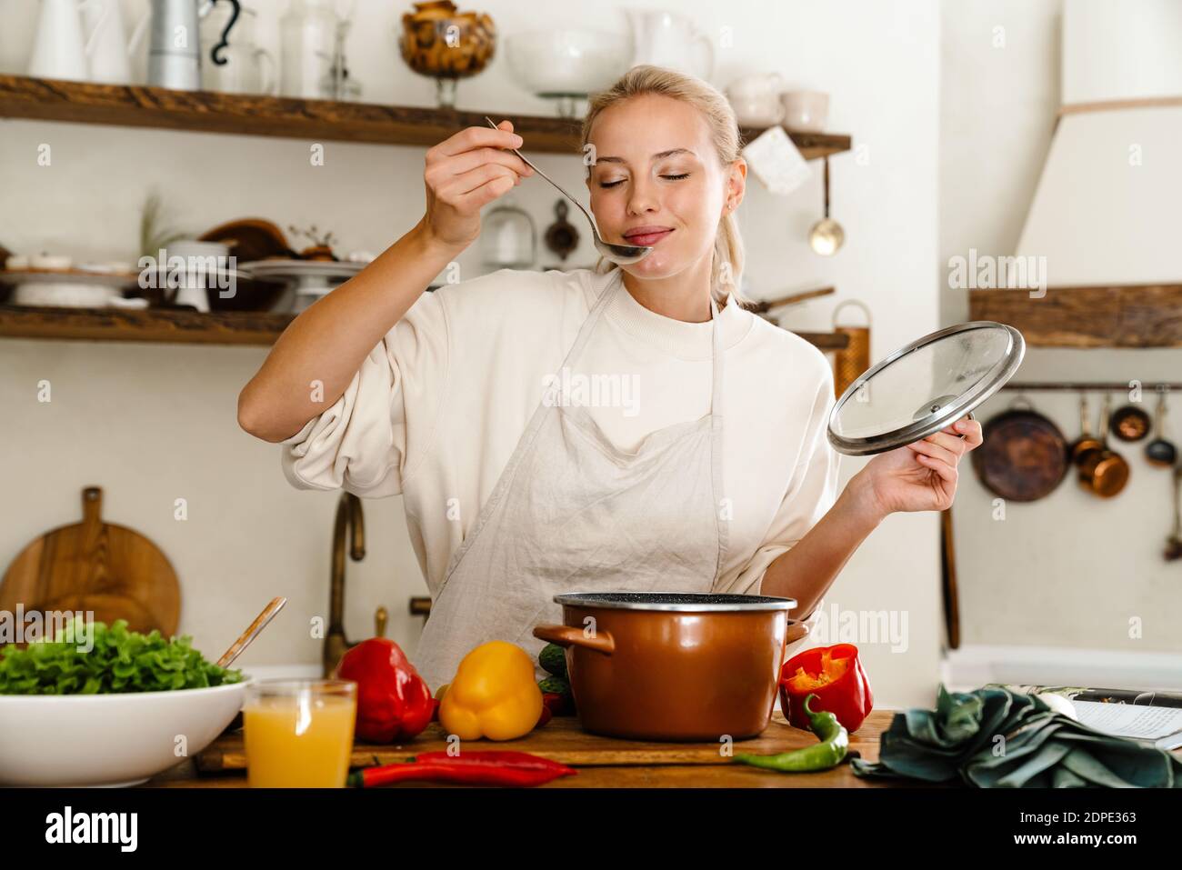 Beautiful pleased woman cooking soup and smiling while making lunch in ...