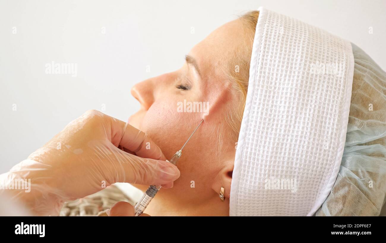 Beautician inserts a long needle with medication under the skin of a ...