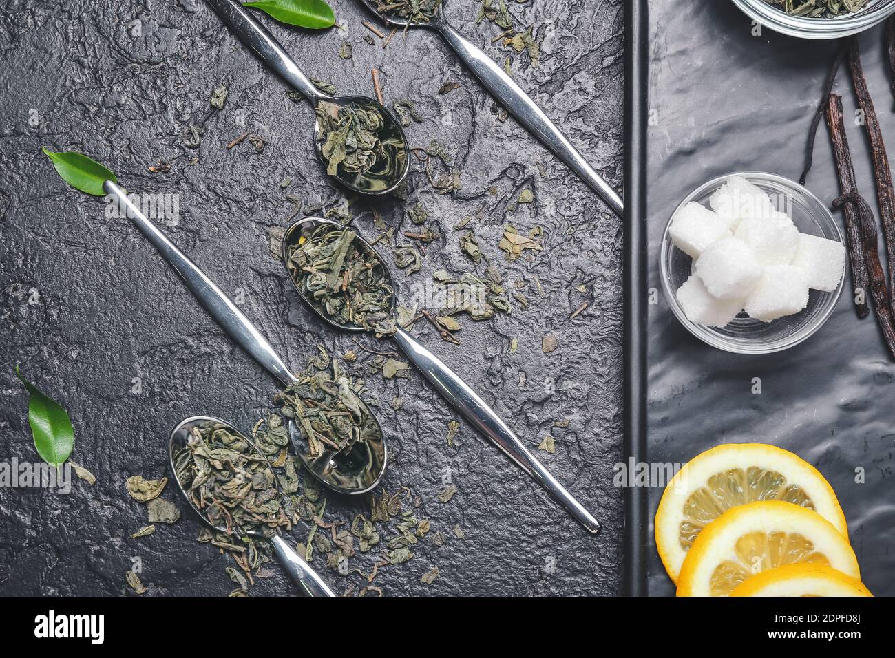 Spoons with dry green tea, sugar and lemon on dark background Stock ...